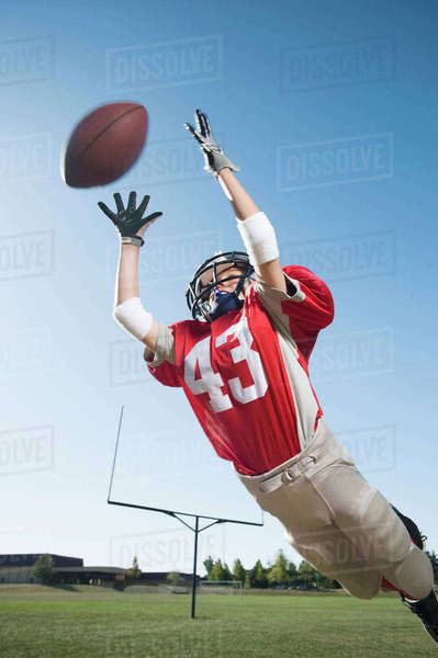 Football player in mid-air reaching for football - Stock Photo - Dissolve