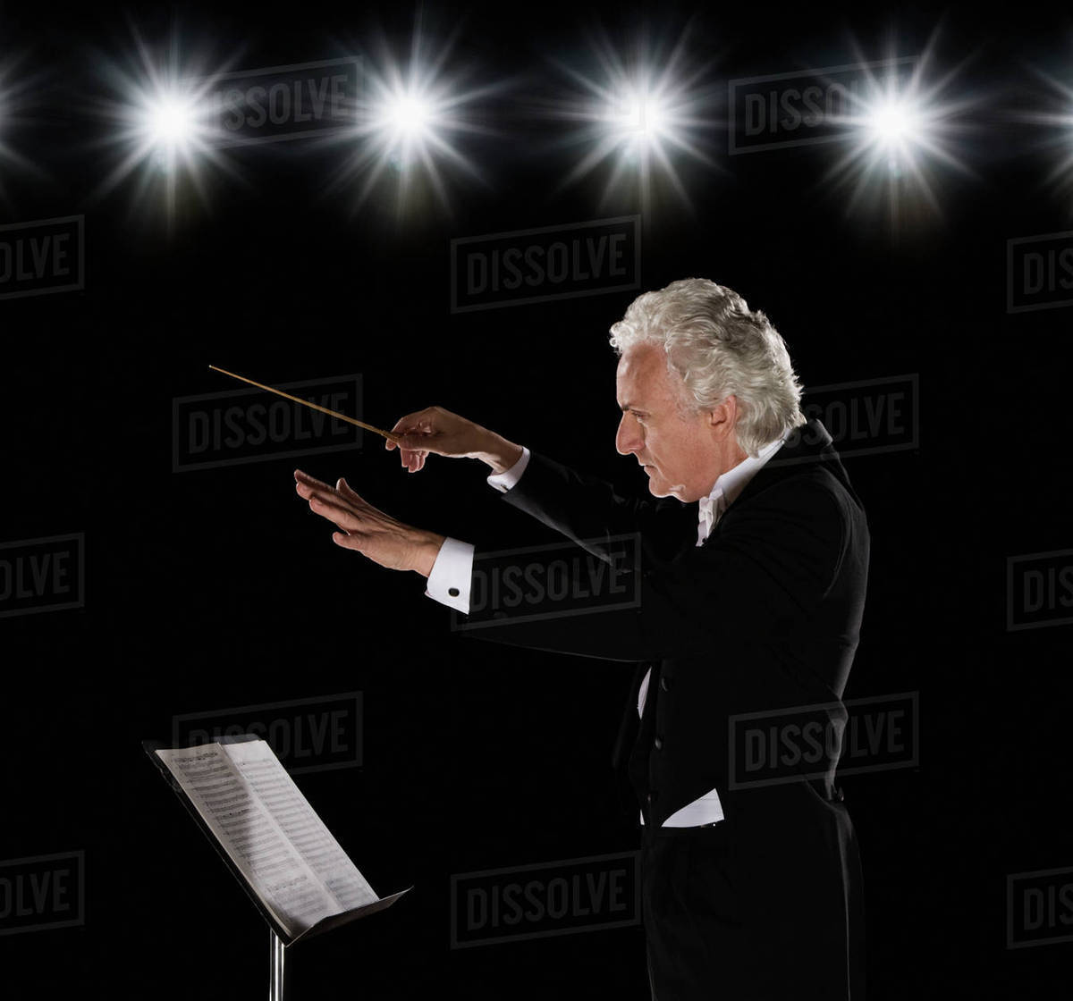 Man in tuxedo conducting under lights - Stock Photo - Dissolve