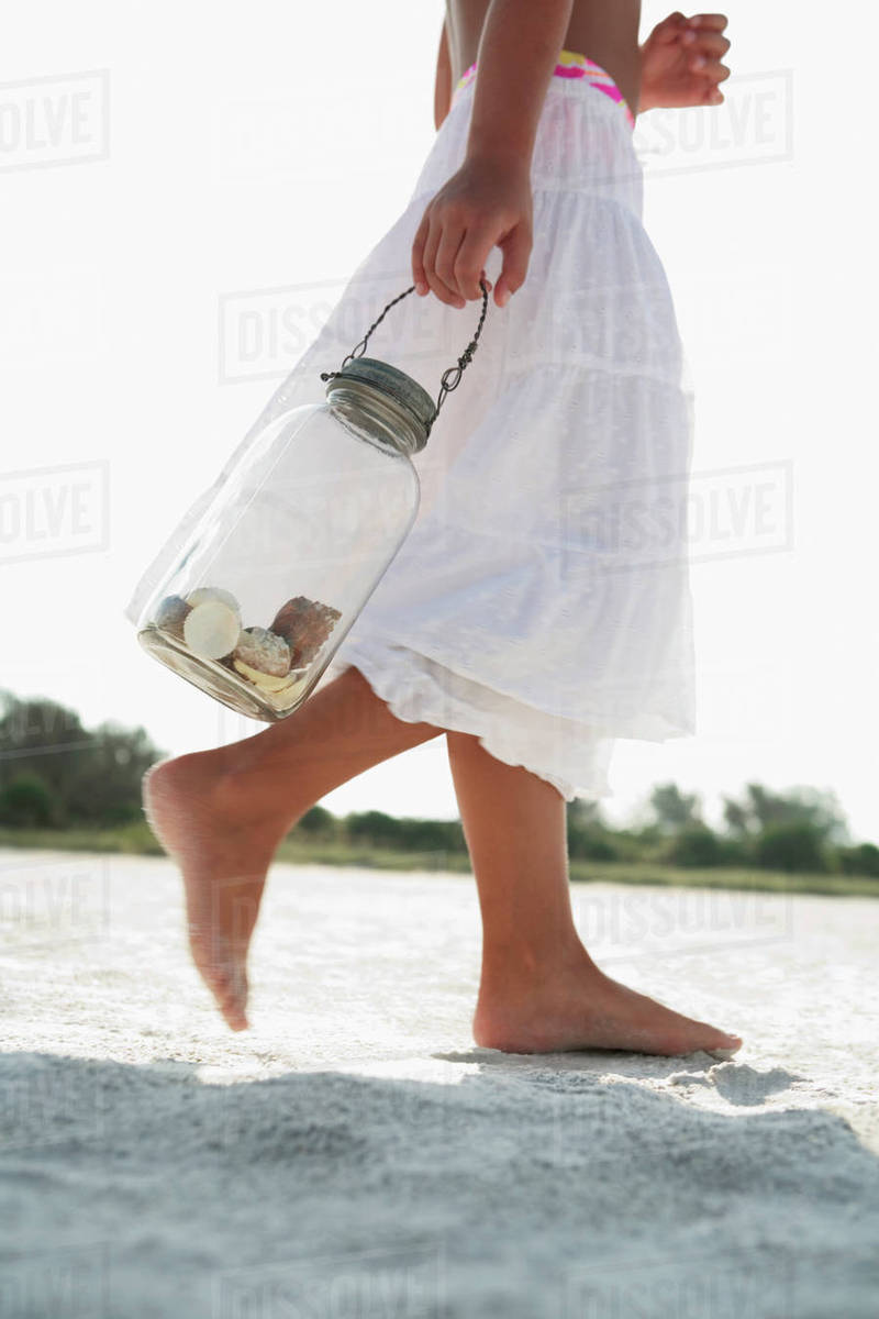 Girl on beach carrying jar of shells - Royalty-free Stock Photo | Dissolve