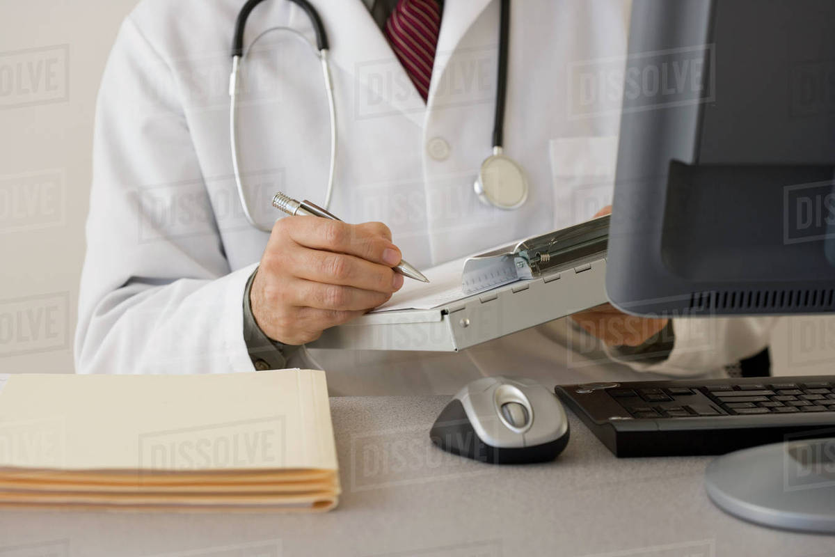 Doctor writing on chart at desk - Royalty-free Stock Photo | Dissolve