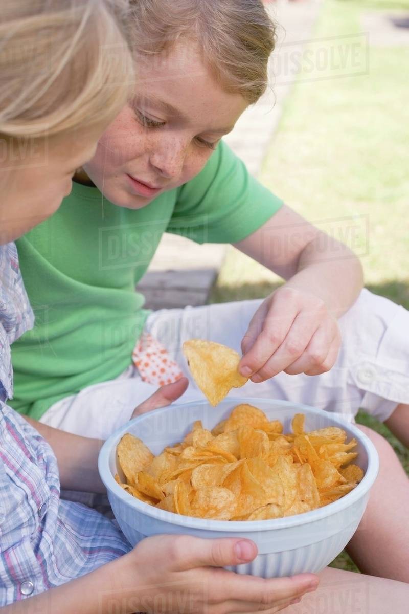 Two girls eating crisps out of doors - Stock Photo - Dissolve