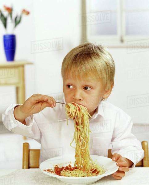 Boy eating spaghetti with tomato sauce - Stock Photo - Dissolve