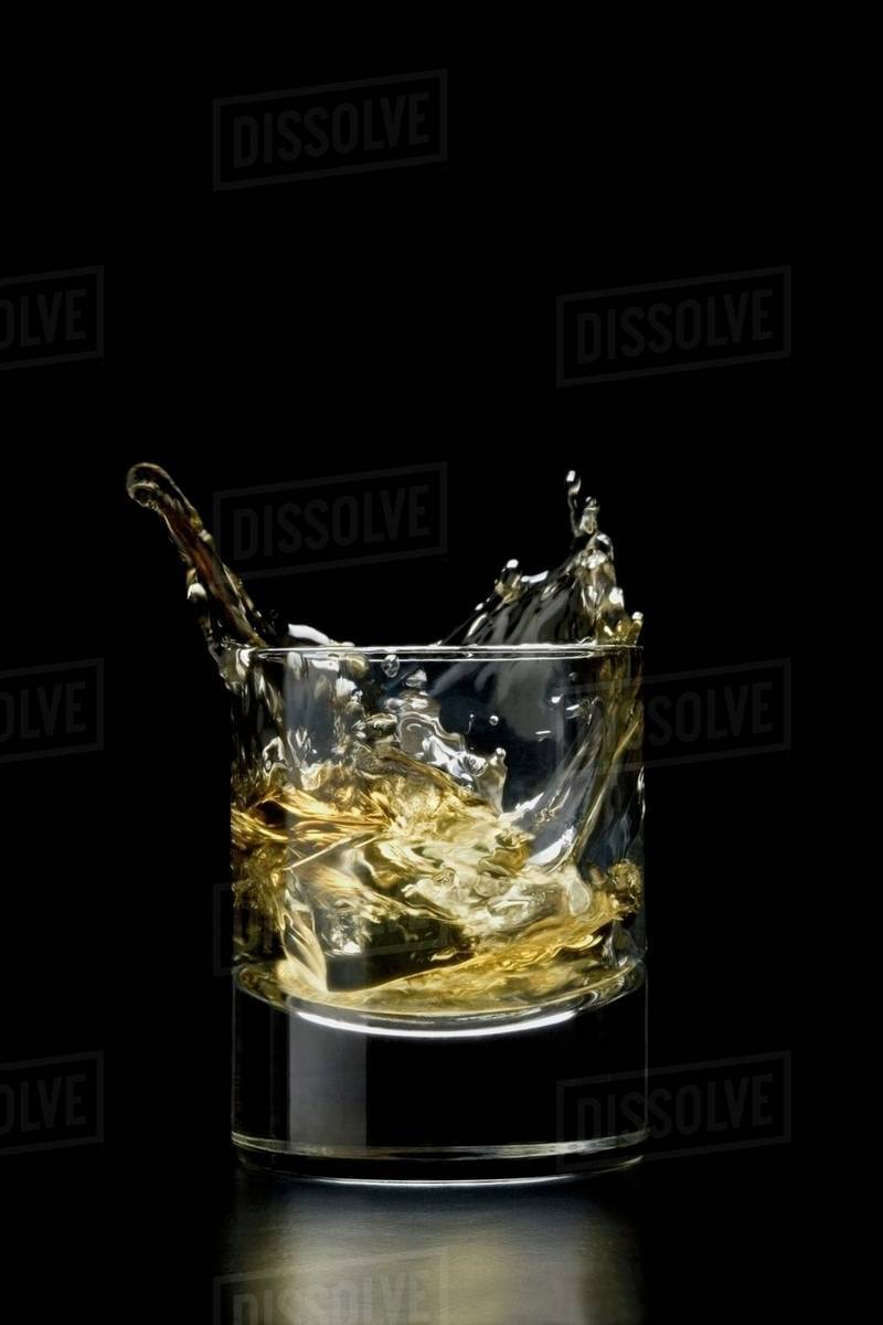 Ice cube falling into a glass of whisky - Stock Photo - Dissolve