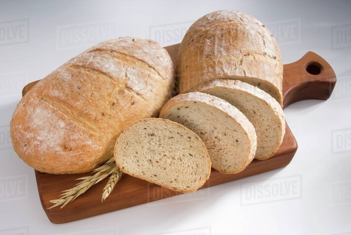 Whole and partly sliced loaves of bread on a wooden board - Stock Photo ...