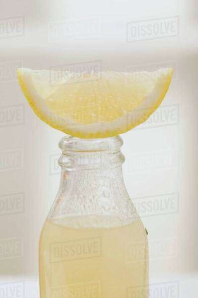 Lemon juice in bottle with fresh lemon wedge - Stock Photo - Dissolve