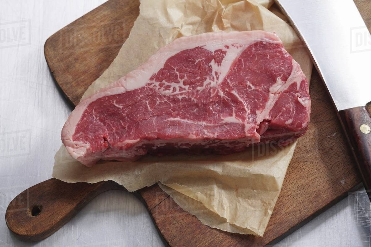 Raw entrecôte on a piece of paper on a chopping board (seen from above ...
