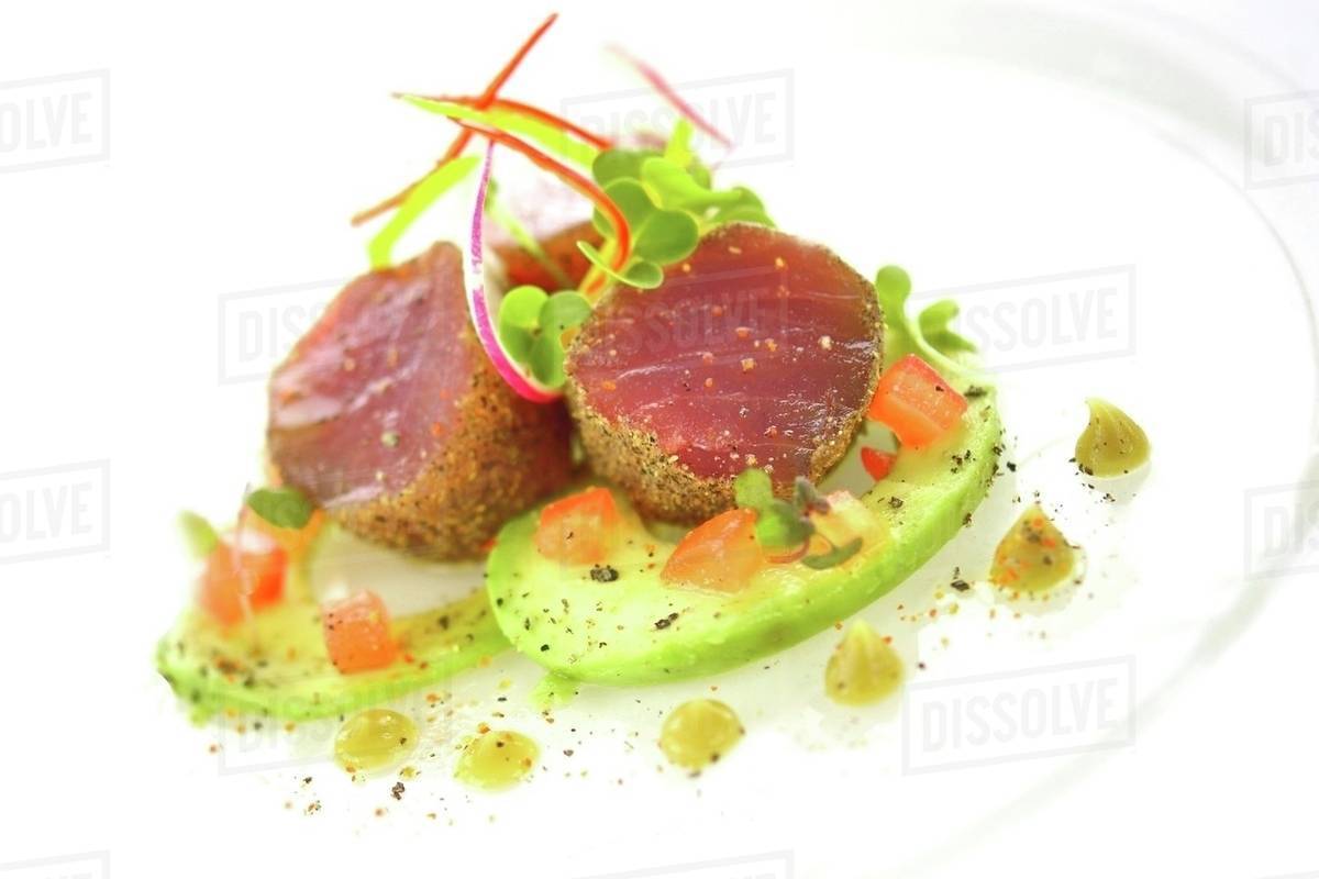 Tuna fish medallions with a crumb crust served with avocado, tomatoes ...