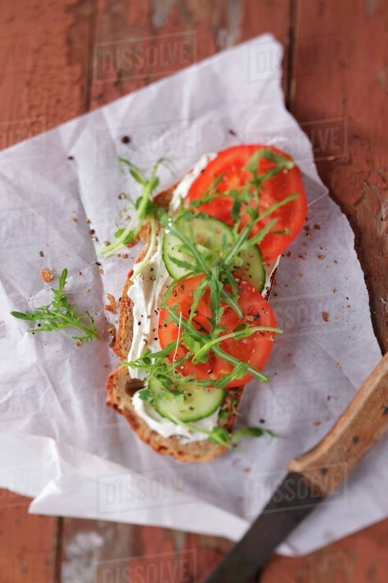 A slice of bread topped with cream cheese, cucumber, tomato and rocket ...