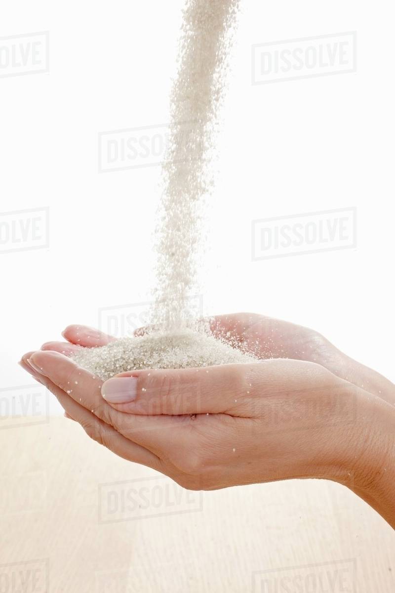 Raw sugar flowing into hands - Stock Photo - Dissolve