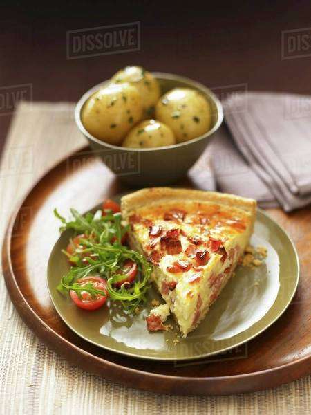 A slice of quiche lorraine with rocket salad and a side dish of ...
