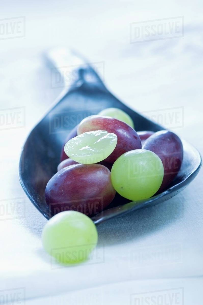 Red and green grapes on a wooden spoon - Stock Photo - Dissolve