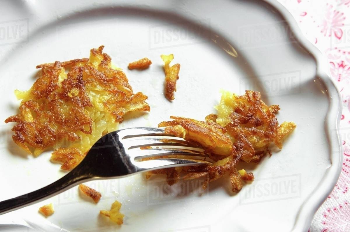A potato rosti (hash brown) on a plate with a fork - Stock Photo - Dissolve