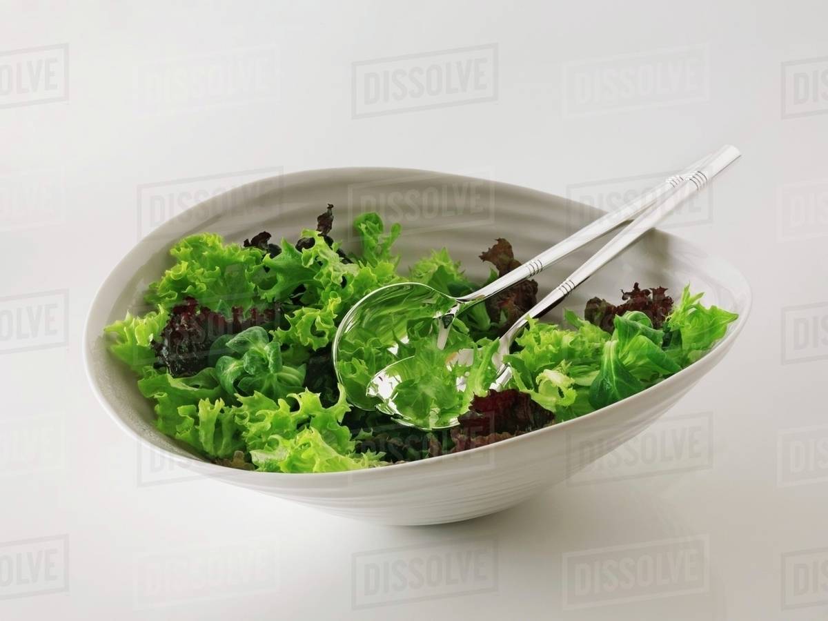 Mixed lettuce in a bowl with salad servers - Stock Photo - Dissolve
