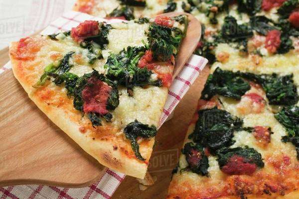 Spinach, tomato and cheese pizza with slice on server - Royalty-free ...