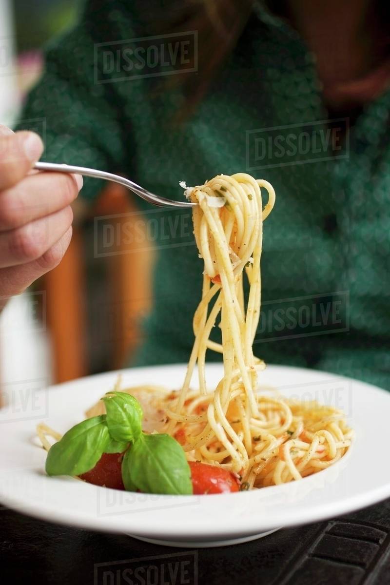 Woman eating spaghetti with tomatoes and basil - Stock Photo - Dissolve