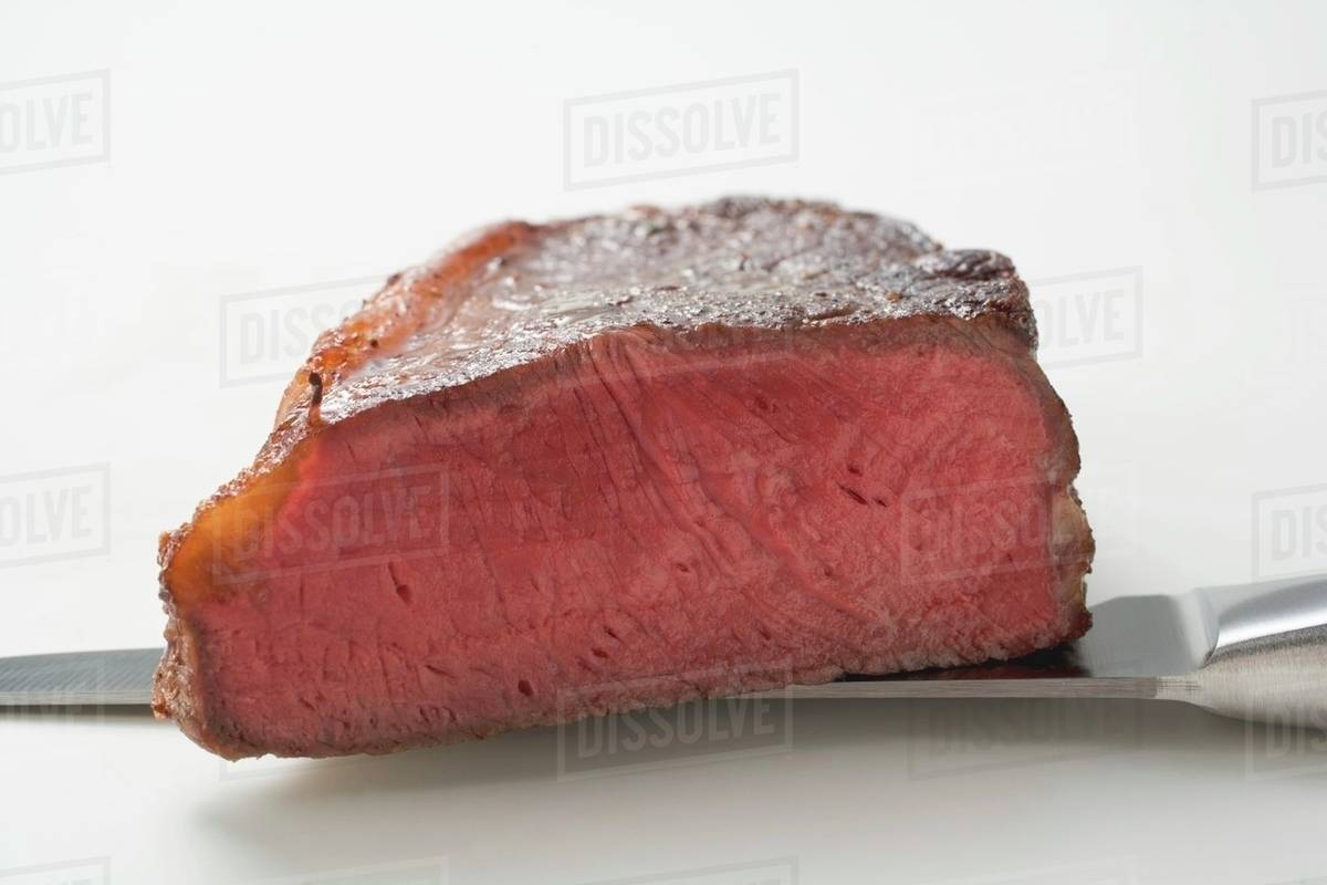 Beef steak, showing cut edge, on knife - Stock Photo - Dissolve