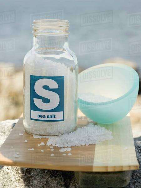 Sea salt in jar on chopping board, sea in background - Stock Photo ...