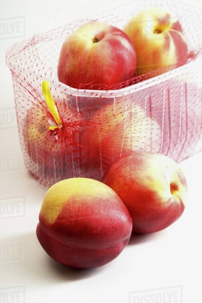 Nectarines in and in front of a plastic punnet with net - Royalty-free ...