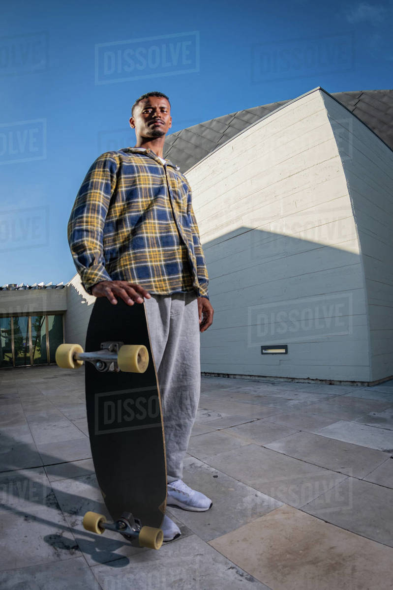 Surf skater posing next to a modern design building during a sunny day ...