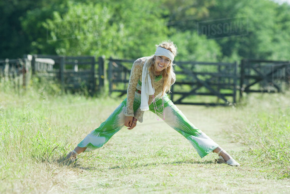 Young woman standing with legs wide apart, in rural field, smiling at ...