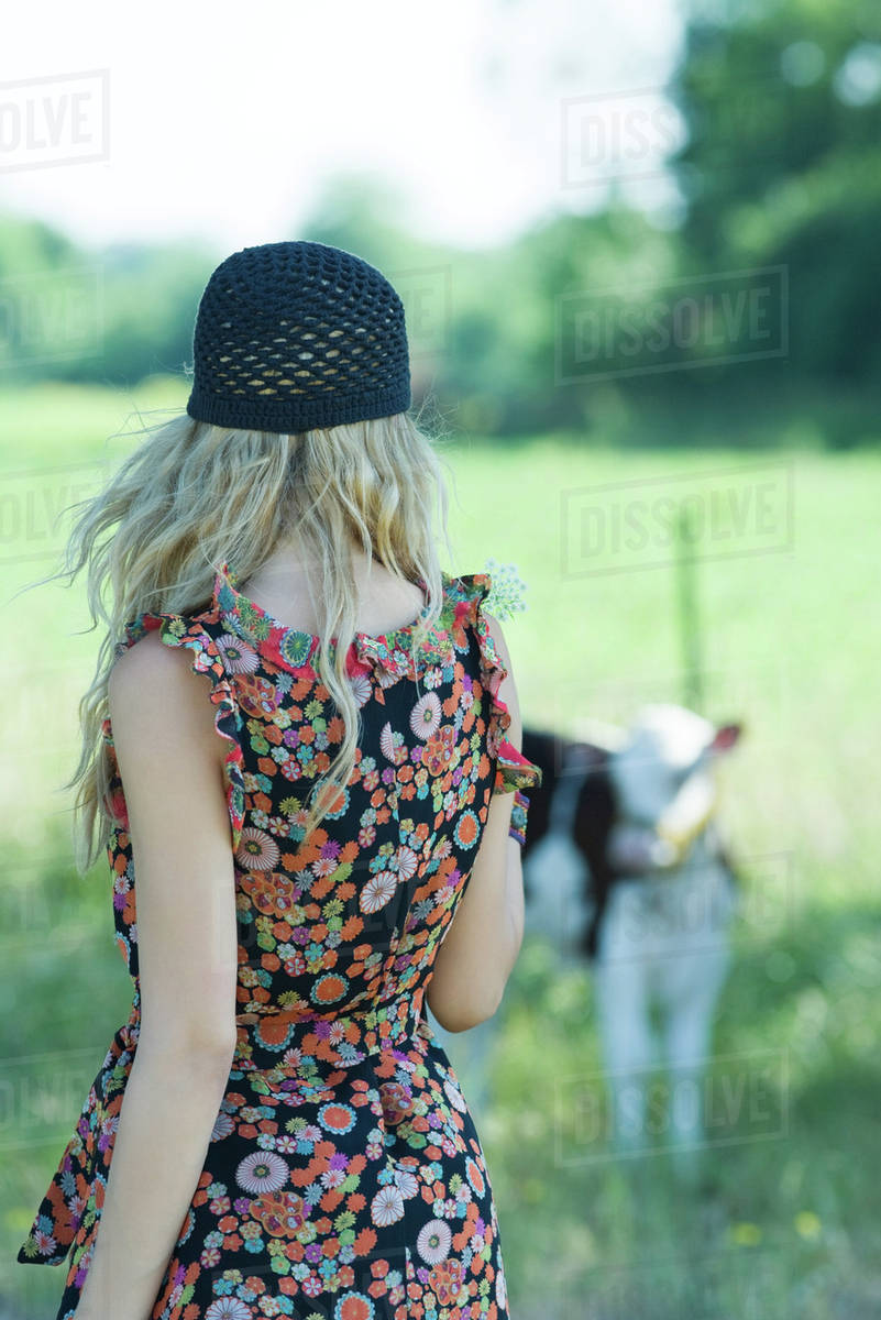 Young woman in sundress walking toward cow, rear view - Royalty-free ...