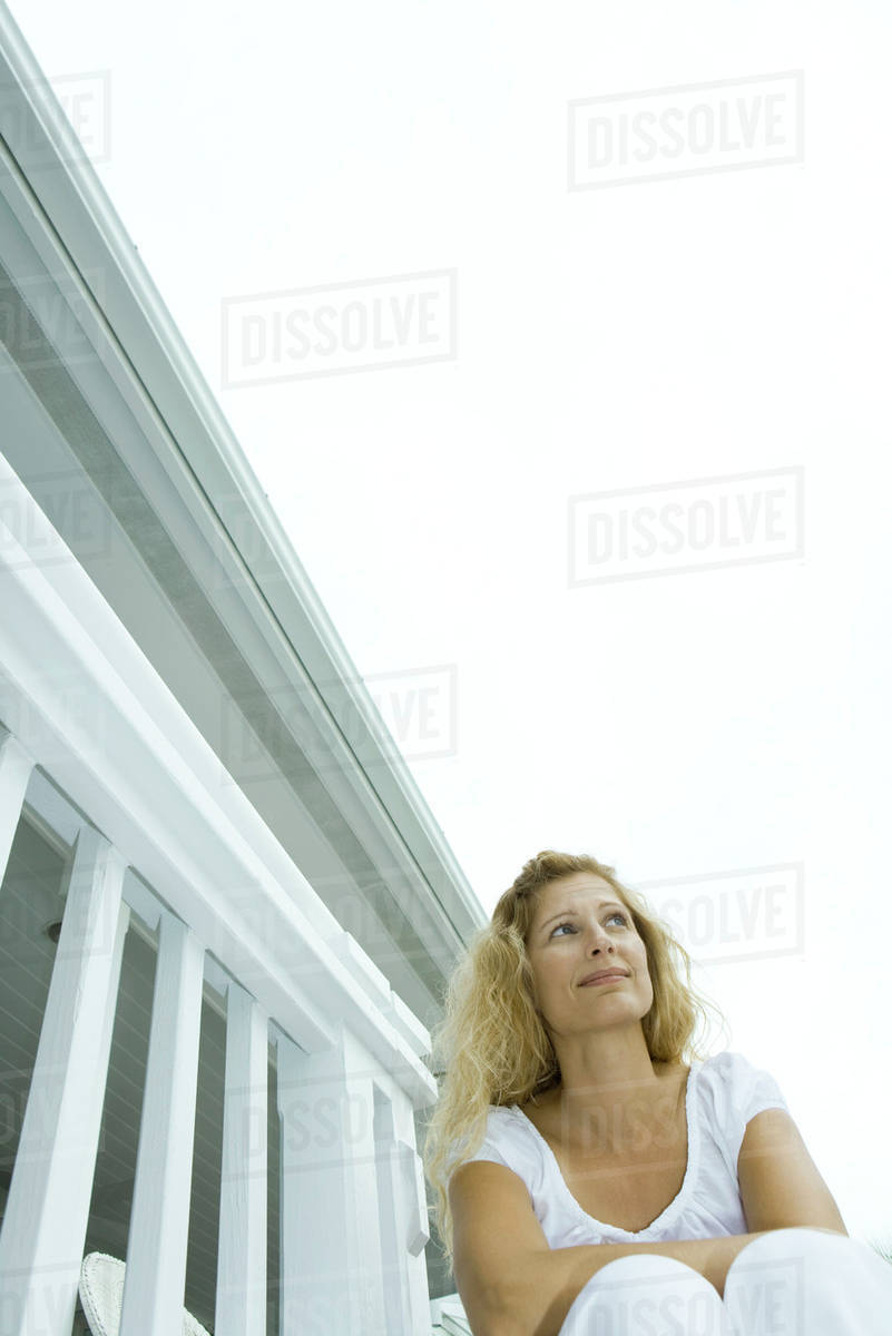 Woman sitting on porch, looking up, low angle view - Stock Photo - Dissolve