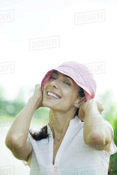 Woman pulling down hat, smiling at camera, portrait - Stock Photo ...