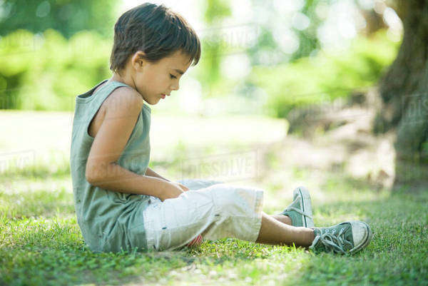 Little boy outdoors, sitting on grass, side view - Stock Photo - Dissolve