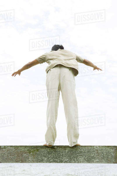 Man standing on ledge with arms out, leaning forward, rear view - Stock ...