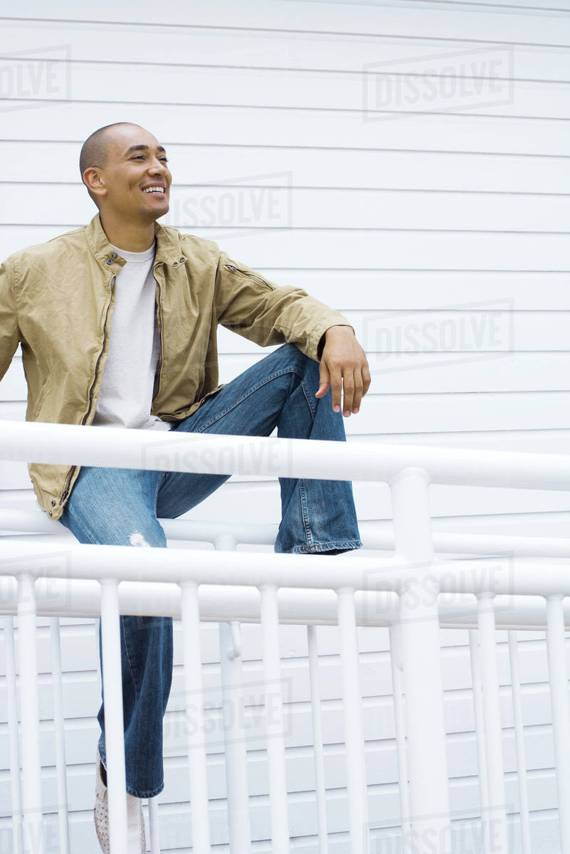 Man sitting on railing, looking away, smiling - Royalty-free Stock ...