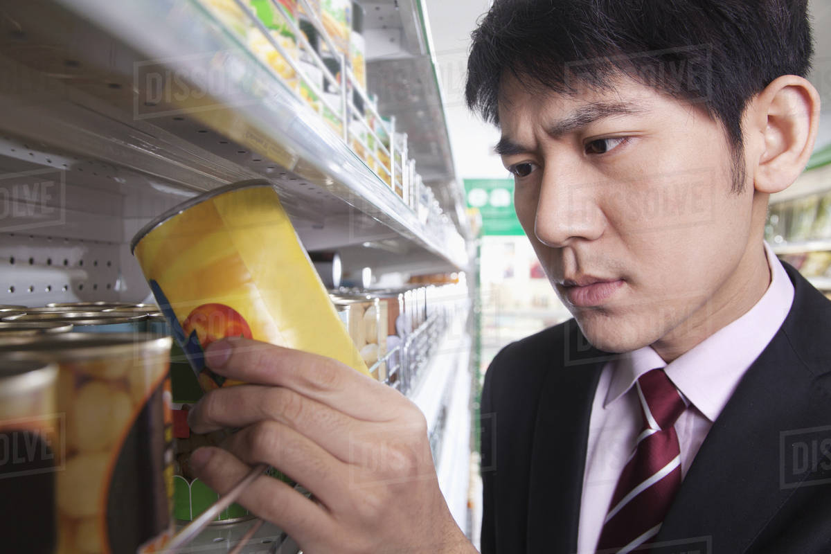 Businessman looking at can in the Supermarket - Stock Photo - Dissolve