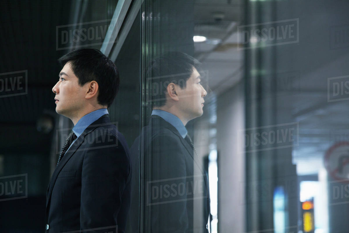 Businessman standing by glass wall, reflection - Stock Photo - Dissolve