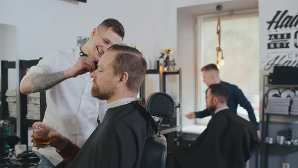 Handsome client drinking whiskey while barber trimming his hair - Stock ...