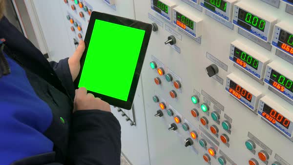 The engineer stands by the control panel holding a tablet with green ...