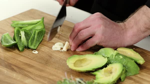 Close-up shot of man's hands cutting clove of garlic into small slices ...