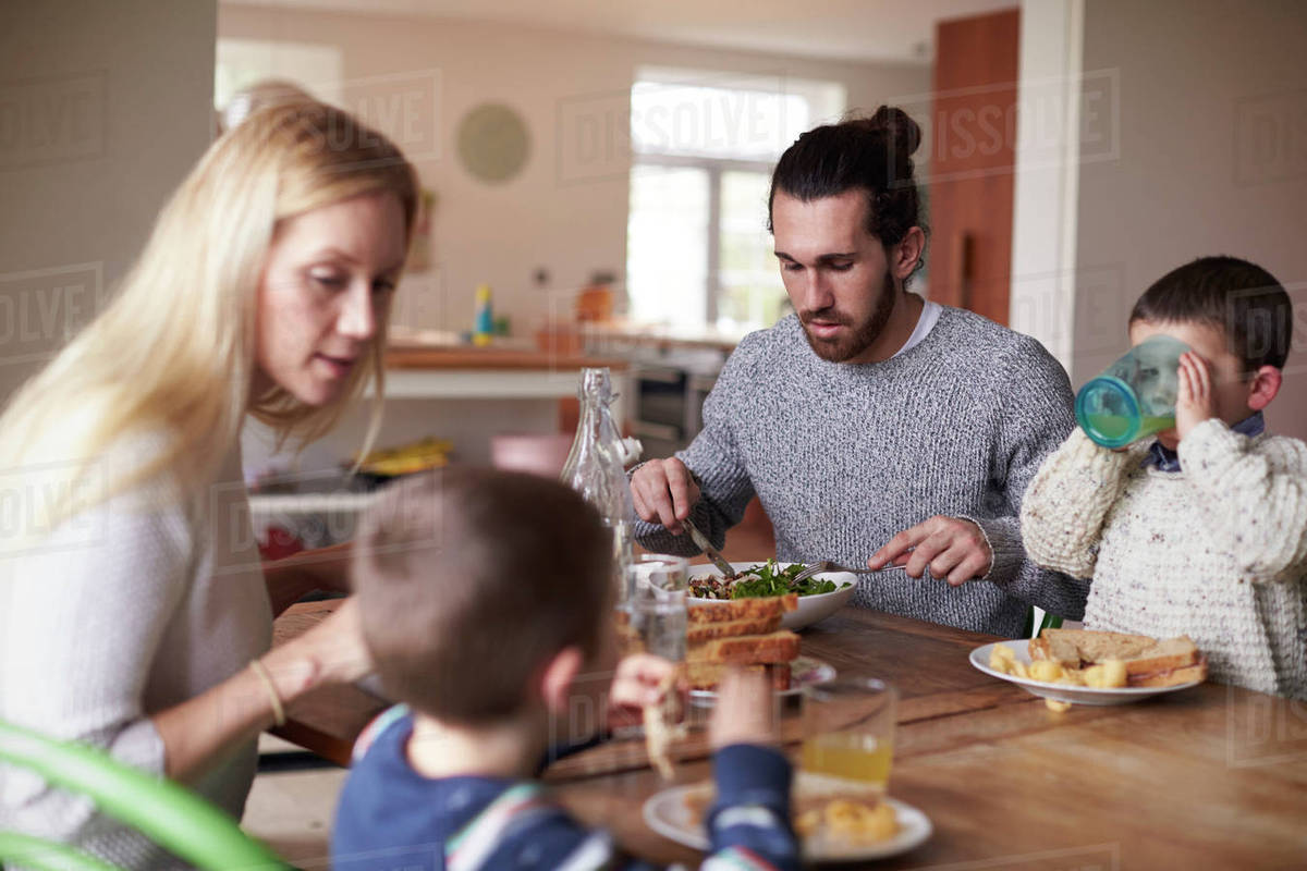 Family sitting at kitchen table and eating meal together - Royalty-free ...