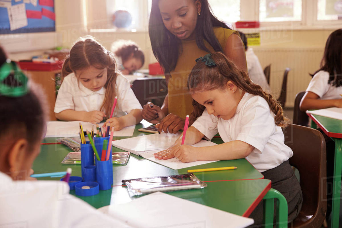 Female elementary school teacher helping pupils at desk - Royalty-free ...