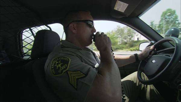 Hand-held shot of a deputy officer having a radio call in patrol car ...