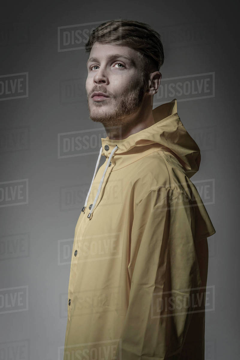 Studio portrait of a bearded young man in a yellow wind cheater ...