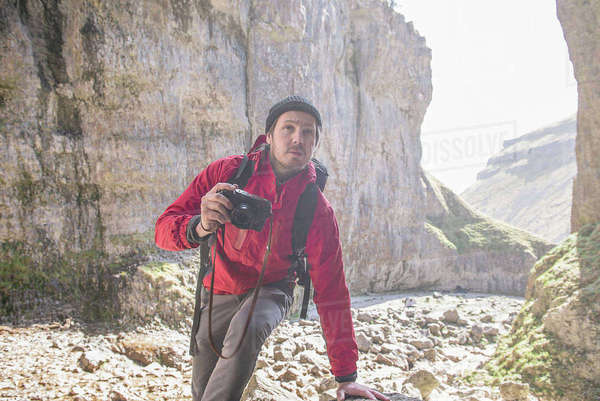 A mountaineer climbing over rocks taking photographs in rugged terrain ...