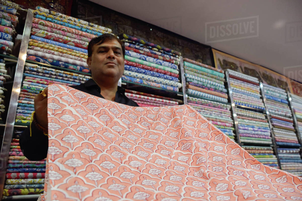 Indian seller showing textiles with variety of colors in shop of a ...