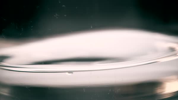 Closeup of clear water liquid being stirred in slow motion in a ...