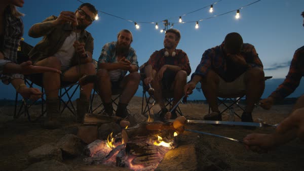 Adult diverse people gathering around burning fire in campsite and ...