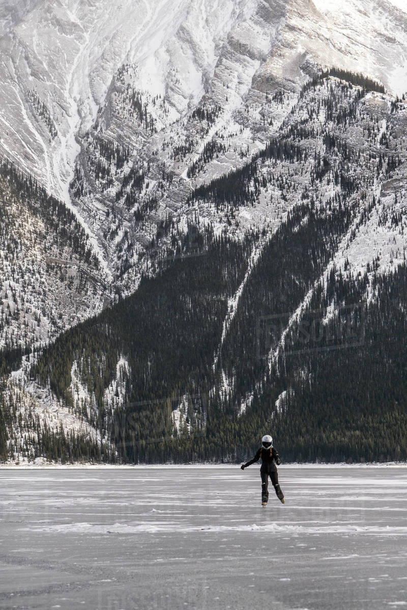 Woman ice skating on frozen lake against snowcapped mountain, Canadian ...