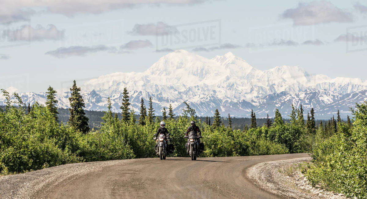 Bikers riding motorbikes on road against snowcapped mountains - Royalty ...