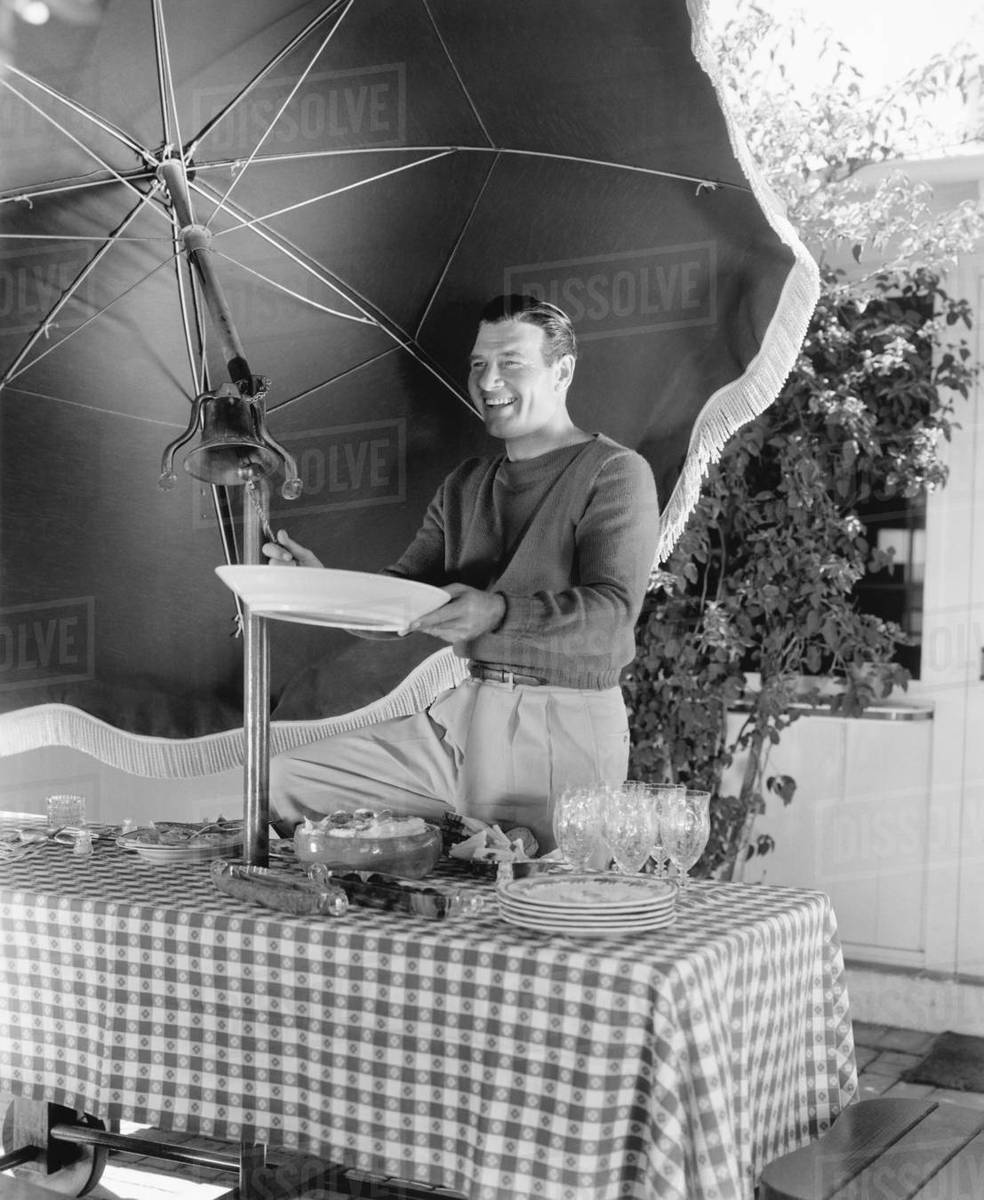 Man standing at a picnic table and holding a plate - Stock Photo - Dissolve