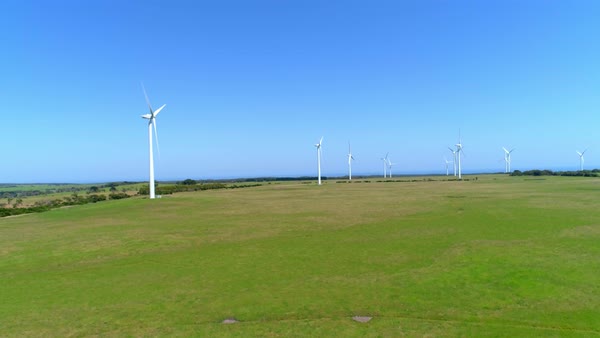 Aerial rise over green grass revealing wind farm on sunny day in ...
