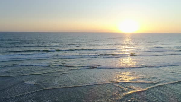 Forward flight towards the sun at sunset over crushing ocean waves ...