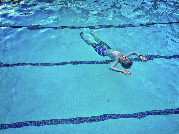 Caucasian boy floating in swimming pool - Stock Photo - Dissolve