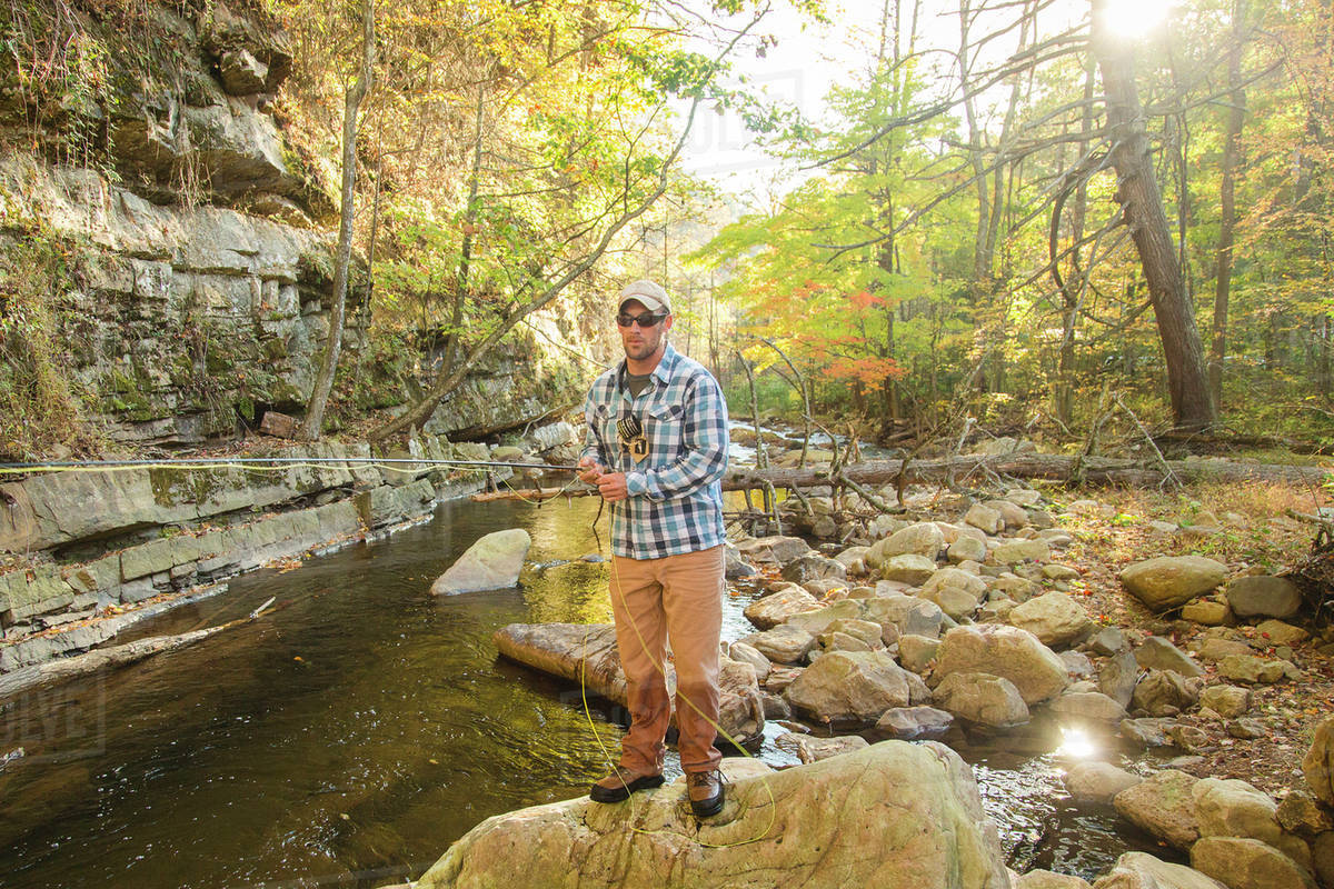 Caucasian man fishing in forest steam - Royalty-free Stock Photo | Dissolve